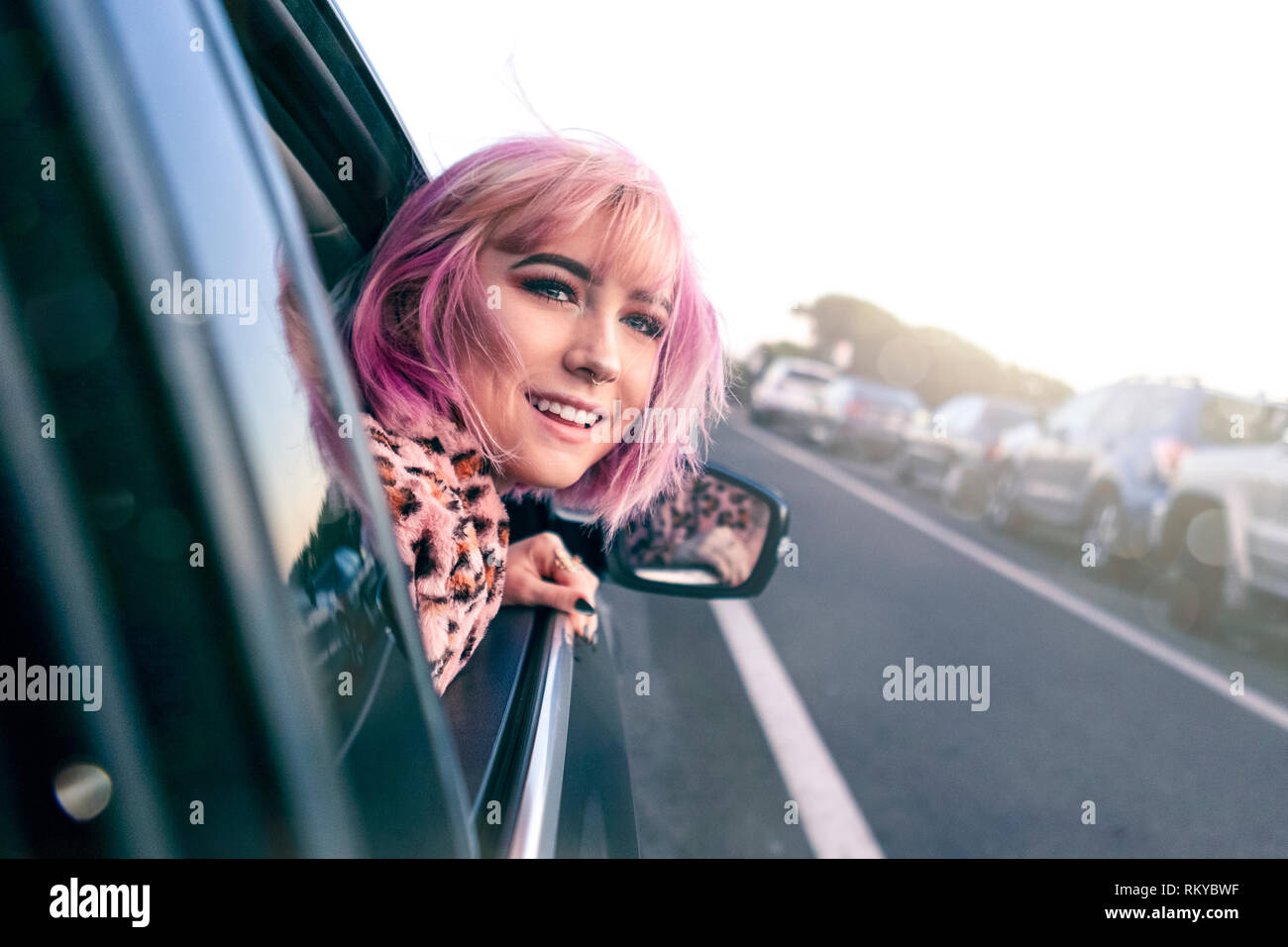 Teen girl with pink hair hangs her head out of a car window on roadtrip ...