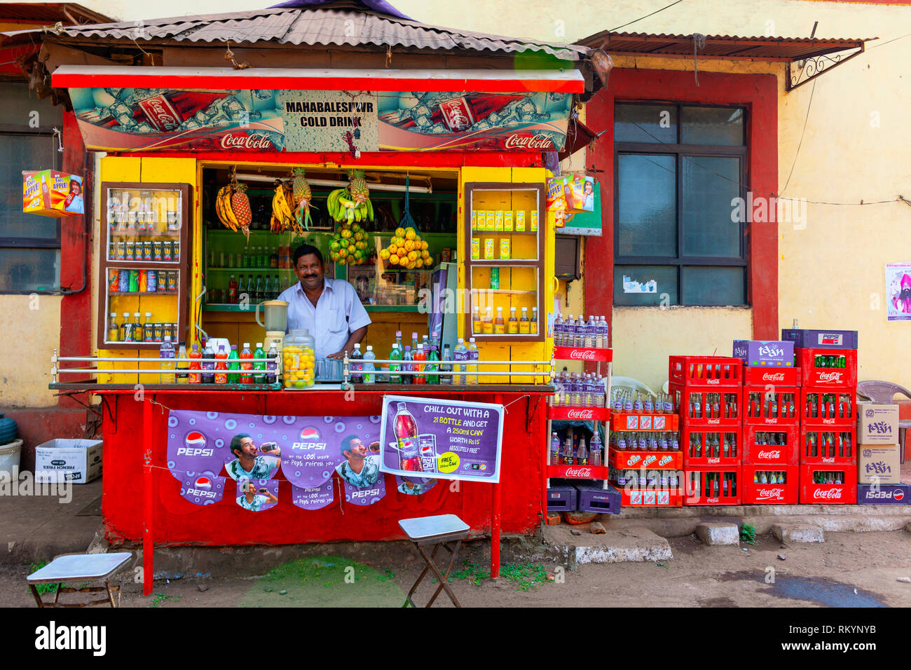 Man selling soft drinks from a brightly coloured street stall in India ...