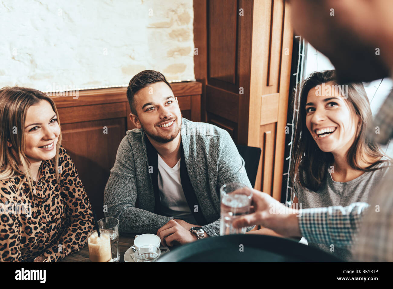A young handsome waiter is serving a group of young smiling friends in ...