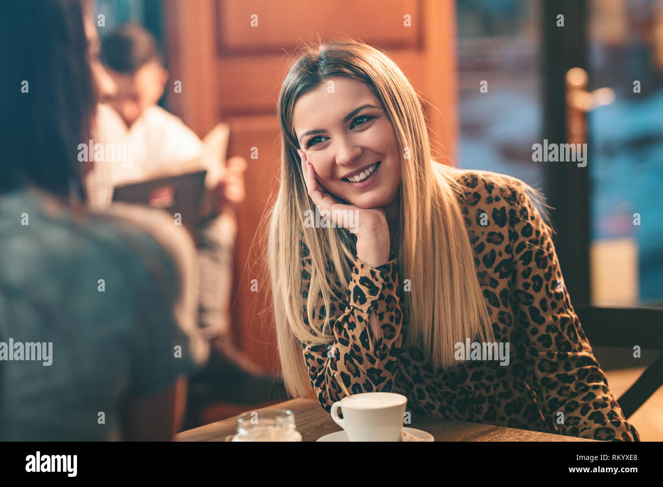 Smiling young woman is sitting with her dear female friend in the cafe ...