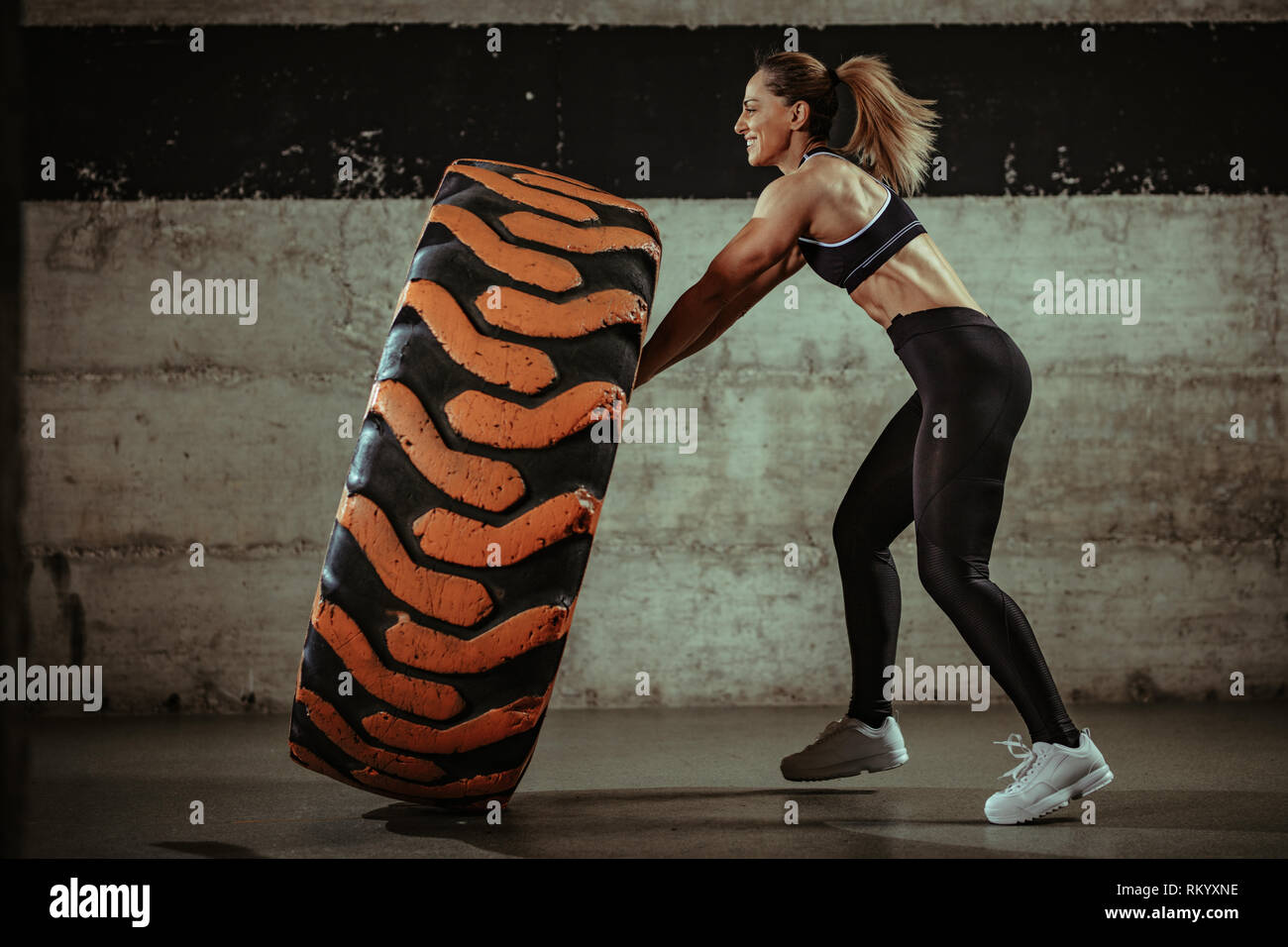 Young muscular woman flipping a wheel tire on training at the gym Stock ...