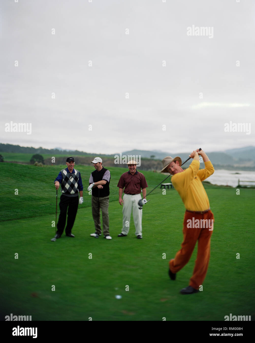 Man taking a swing with a golf club while playing golf with his friends ...
