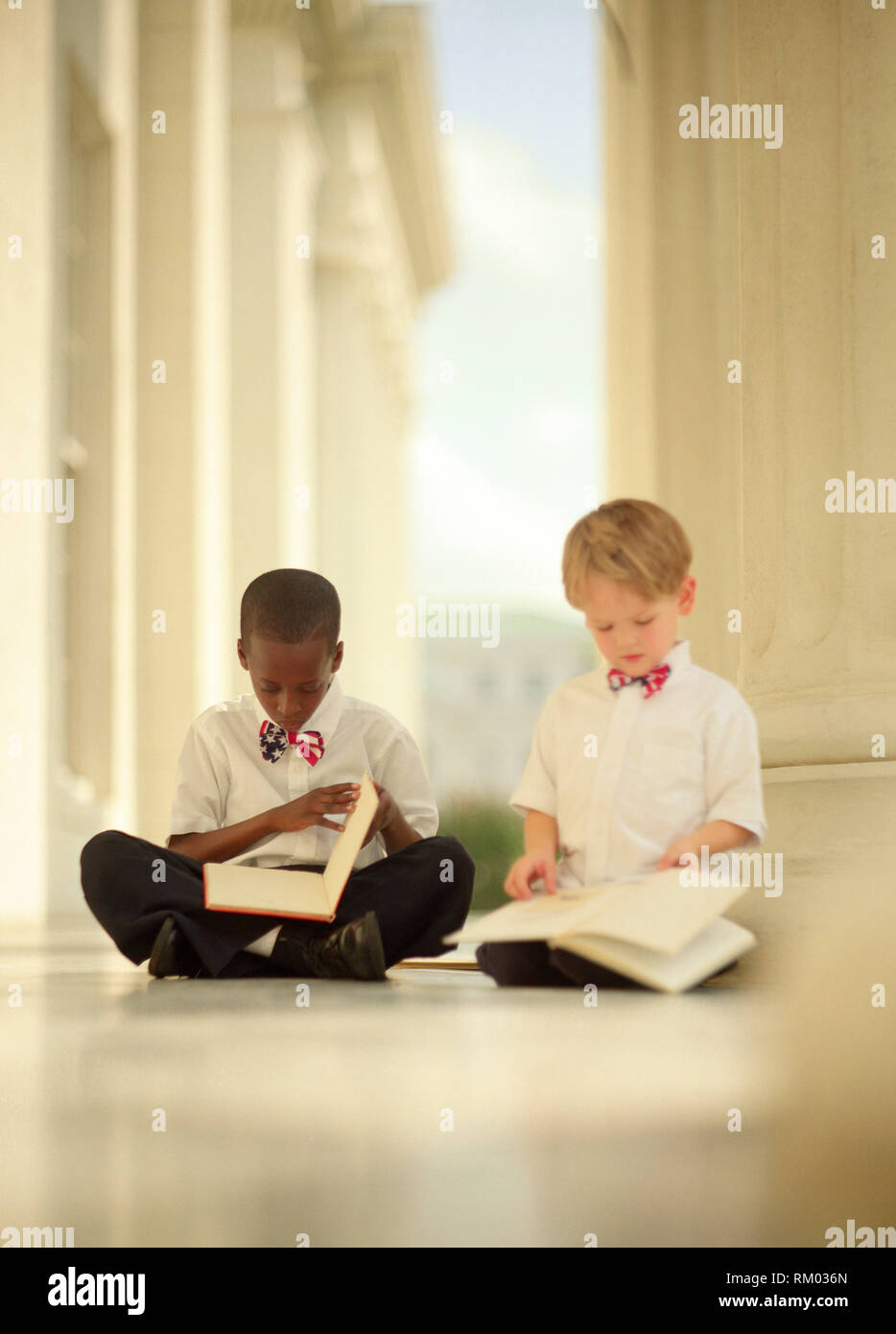 Two young students sitting on the ground reading books Stock Photo - Alamy