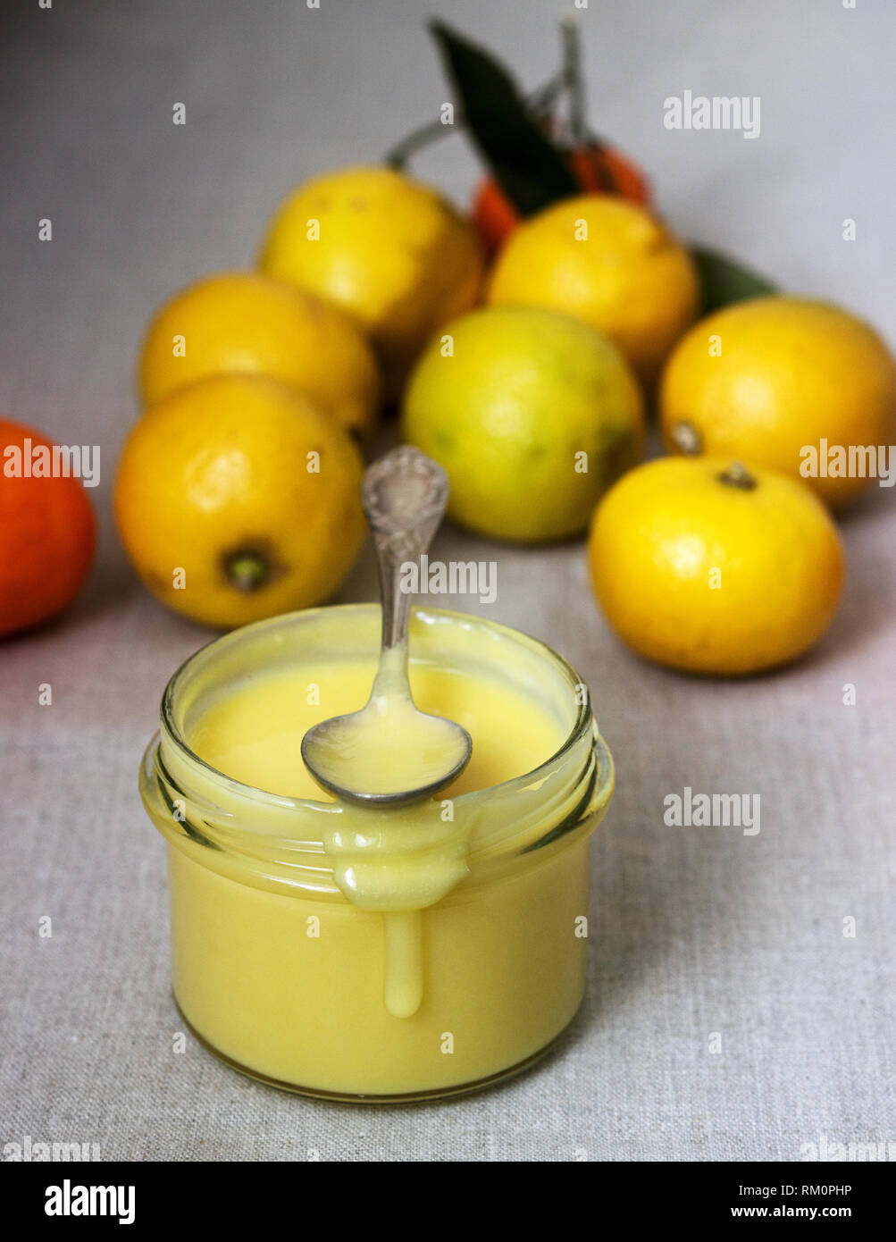 A citrus curd in a glass jar and citrus fruits on a linen tablecloth ...