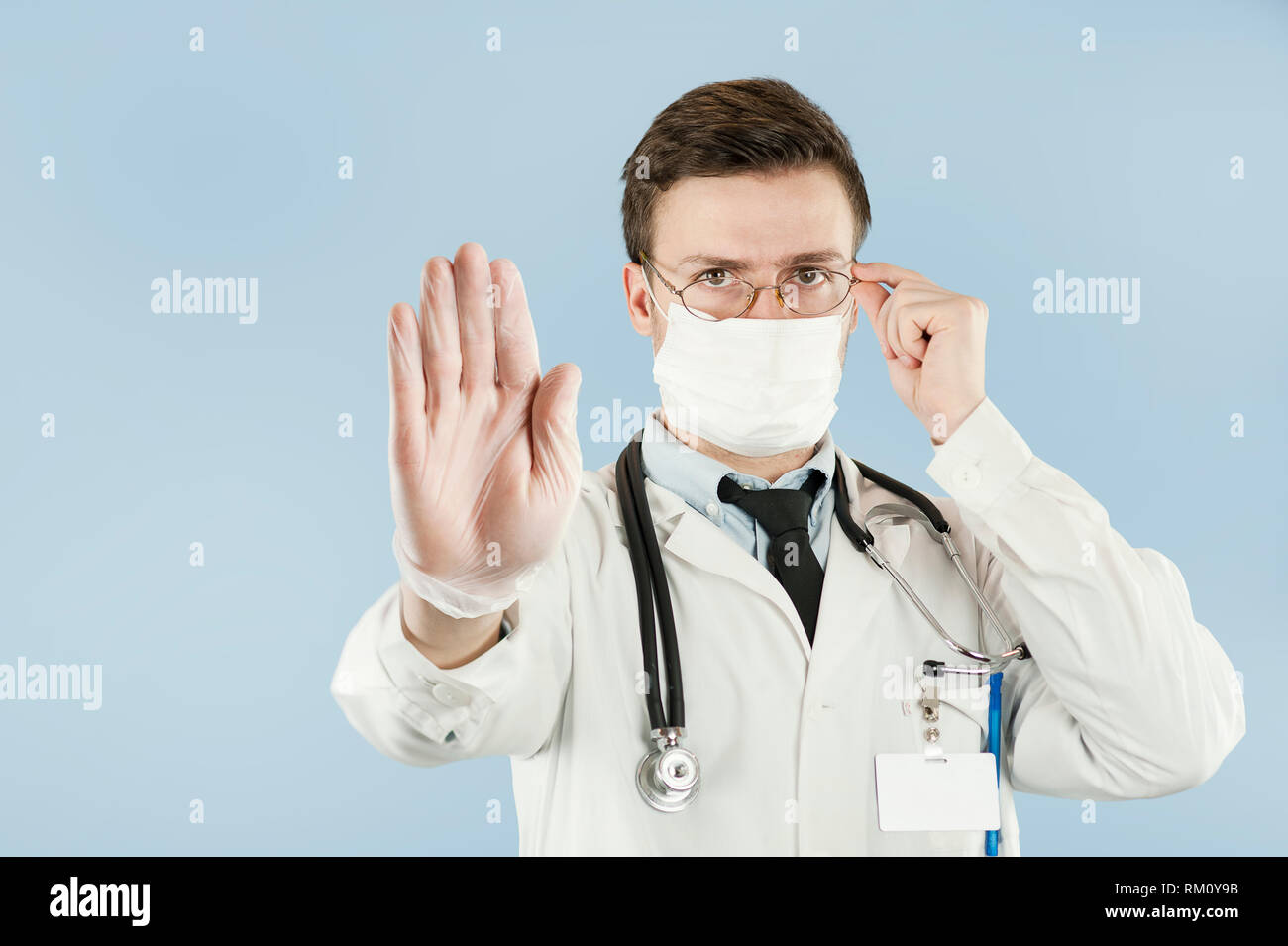 Young guy doctor shows with hand palm stop sign on a blue isolated ...