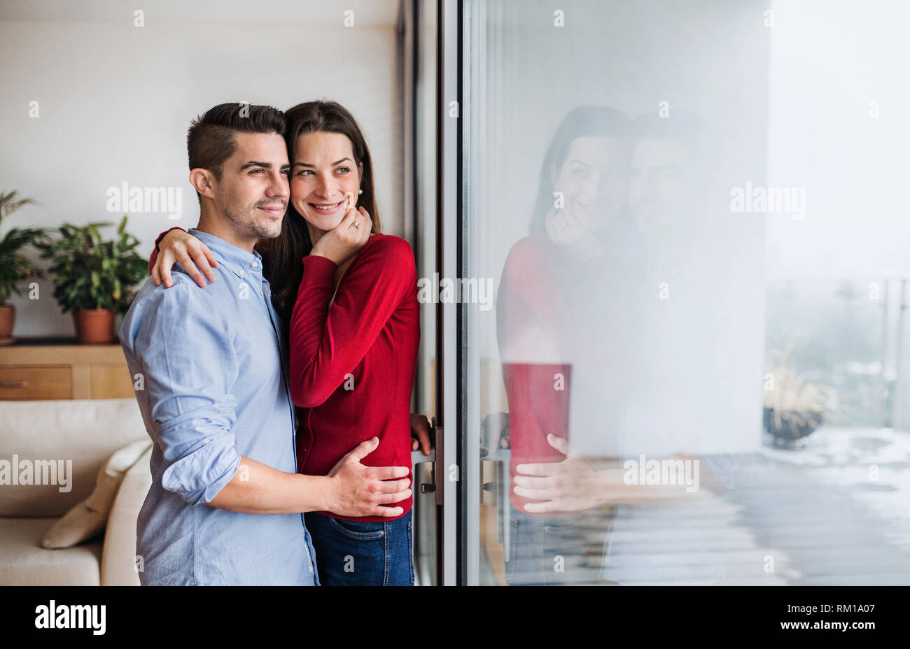 Young couple in love standing by the window at home, hugging. Copy ...