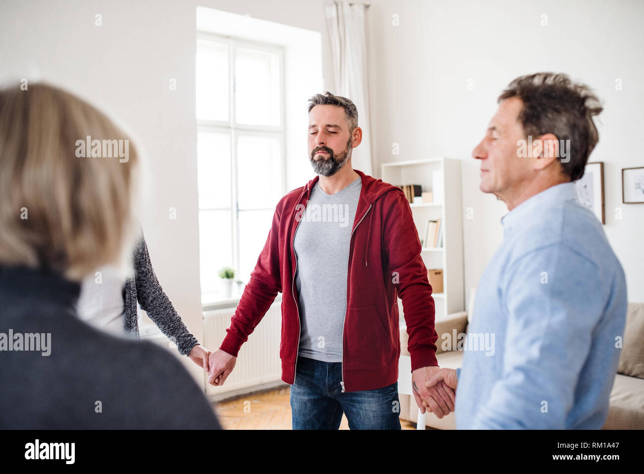 Group of people with closed eyes standing in a circle and holding hands ...