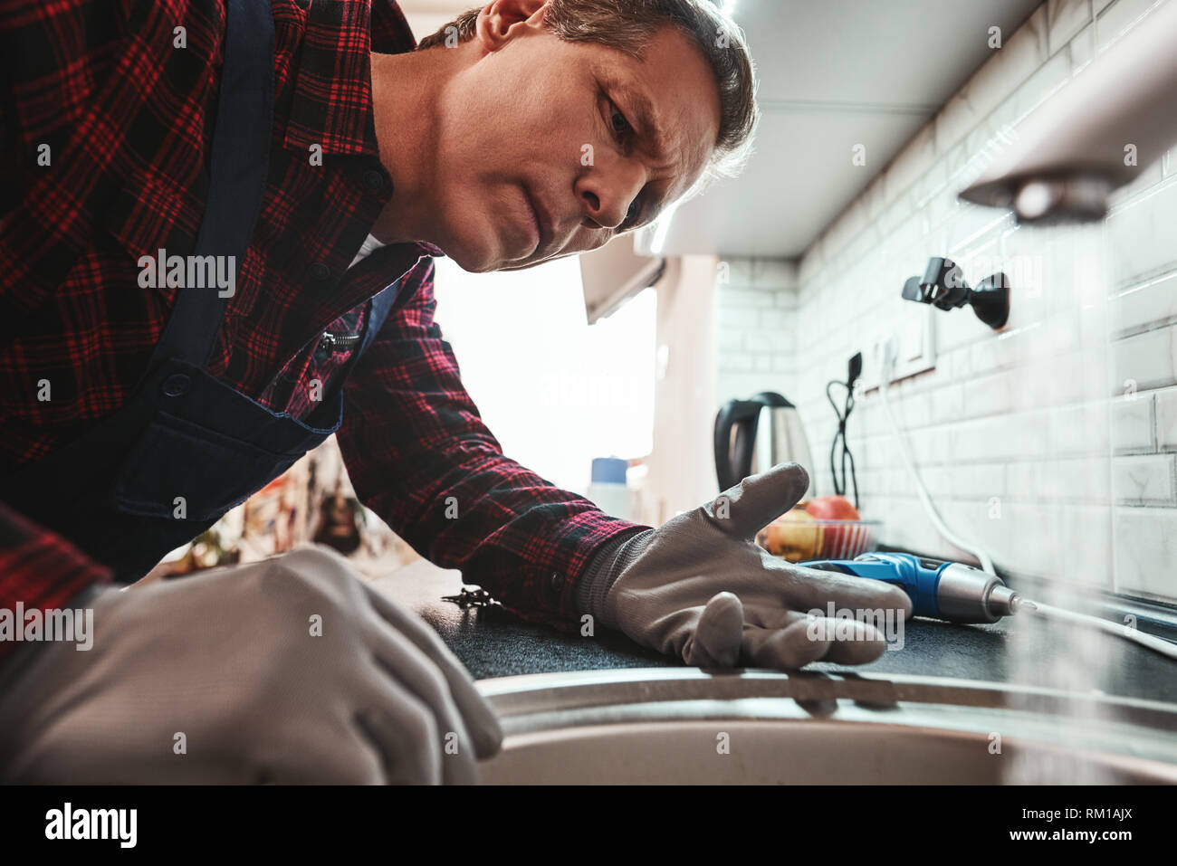 Inside view. Close-up of handsome plumber repairing sink in kitchen ...
