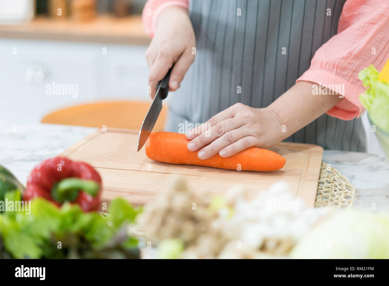 Hand with knife cutting carrot. Woman prepares food at table. Chef ...