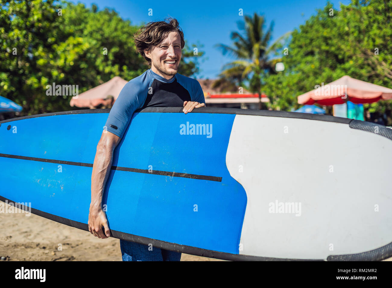 Handsome sporty young surfer posing with his surfboard under his arm in ...
