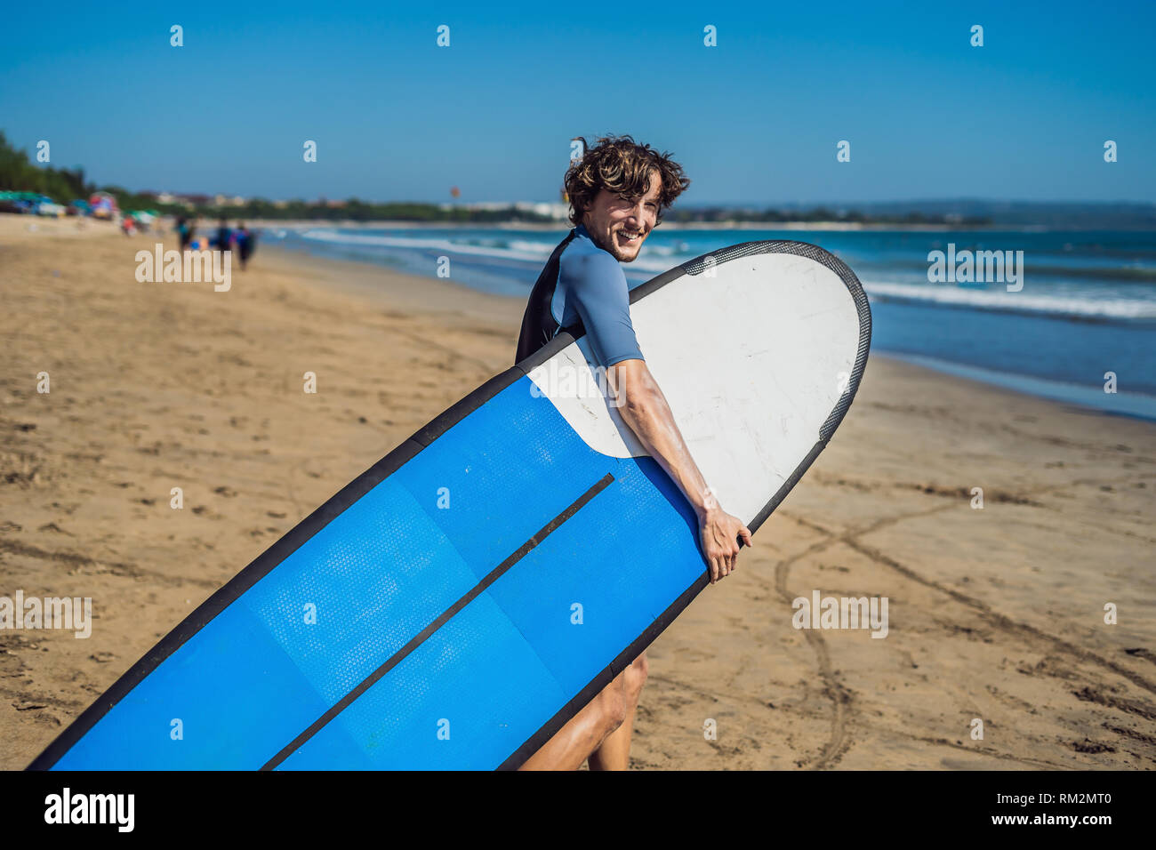 Handsome sporty young surfer posing with his surfboard under his arm in ...