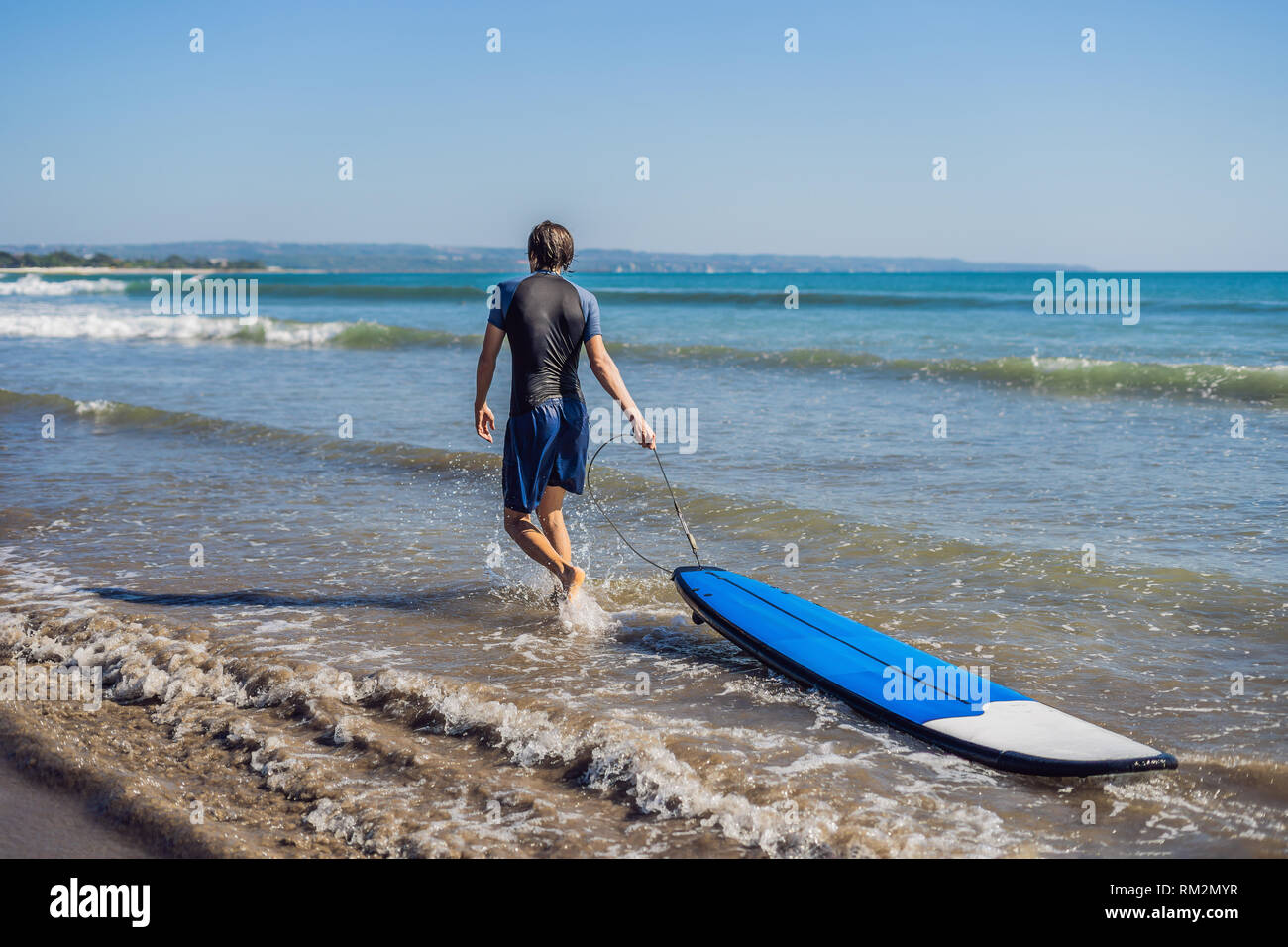 Handsome sporty young surfer posing with his surfboard under his arm in ...