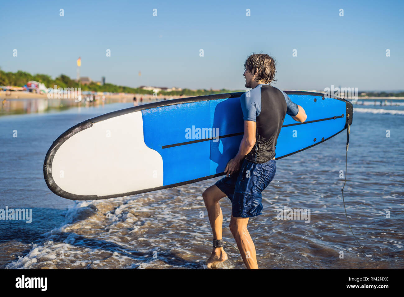 Handsome sporty young surfer posing with his surfboard under his arm in ...