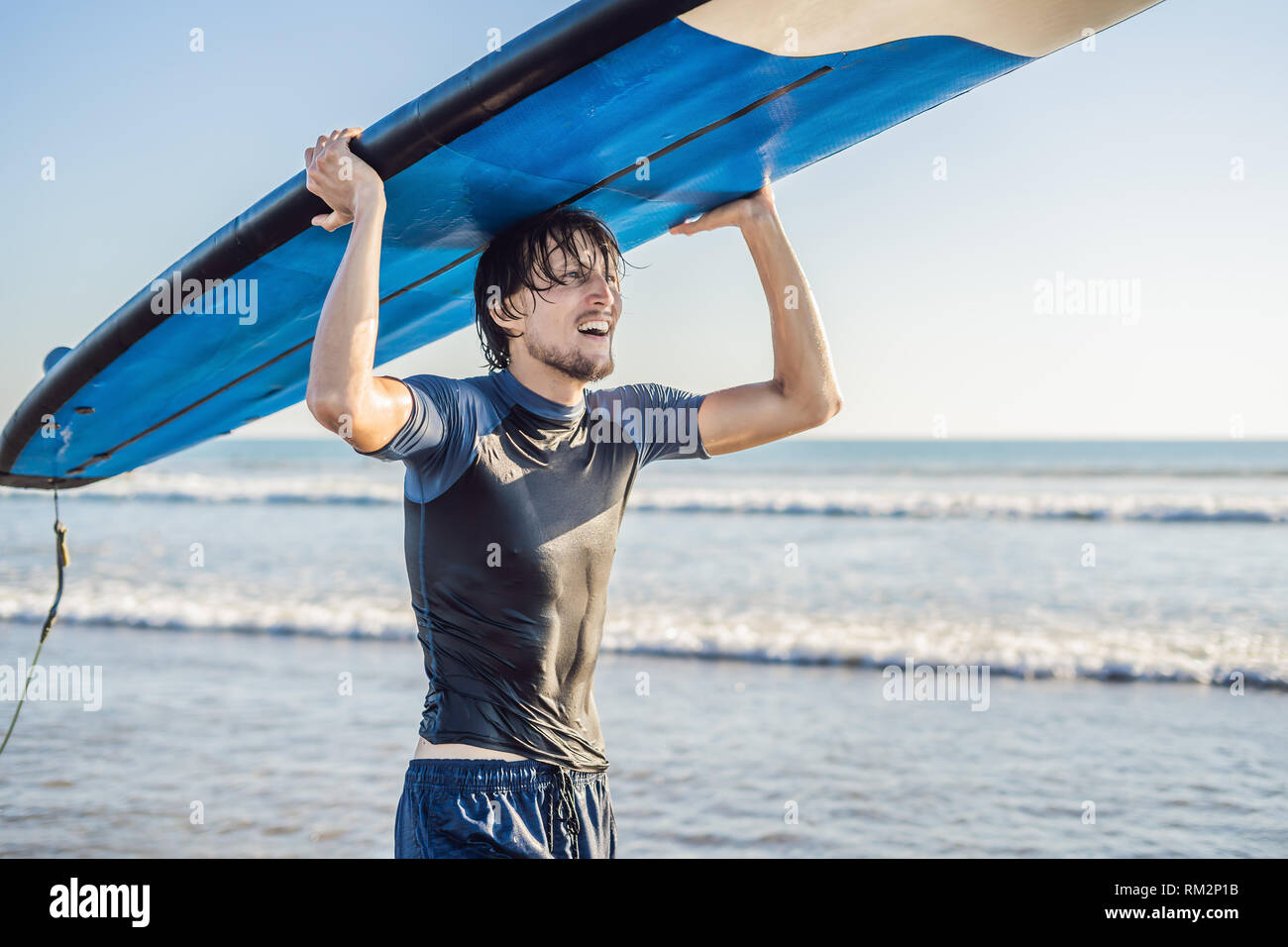 Man carrying surfboard over his head. Close up of handsome guy with ...