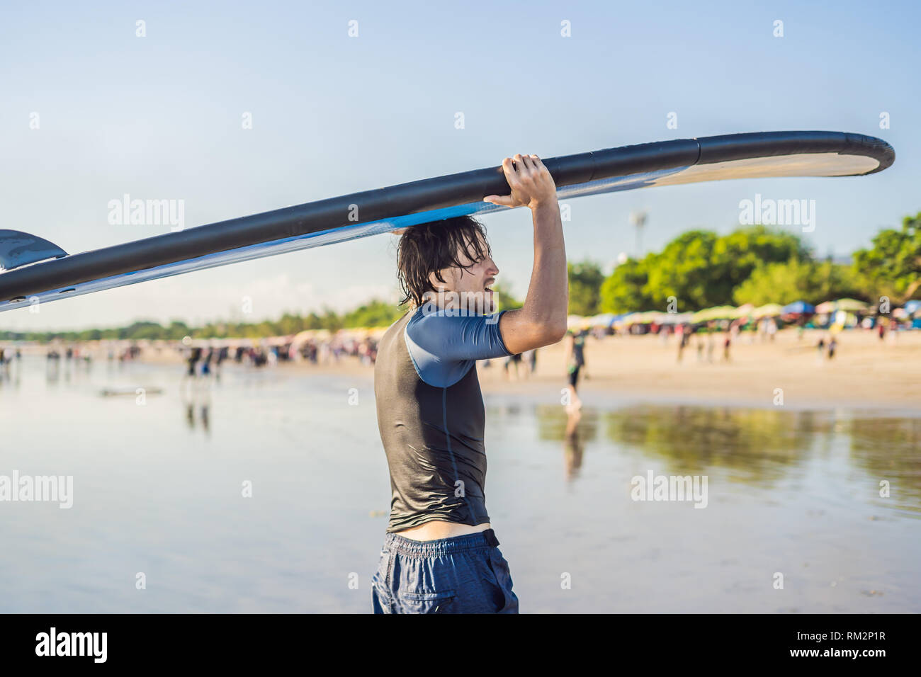 Man carrying surfboard over his head. Close up of handsome guy with ...