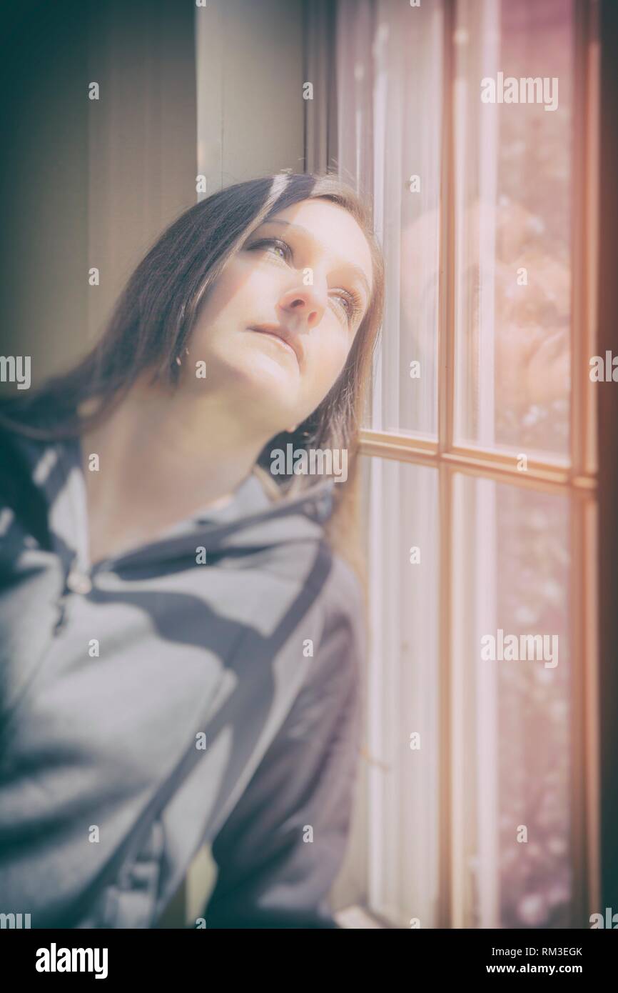 Young woman leaning against a window Stock Photo - Alamy