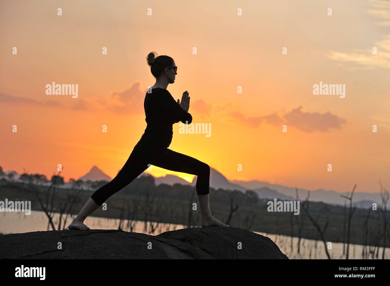 young woman practising yoga posture by the Senanayake Samudraya Lake ...