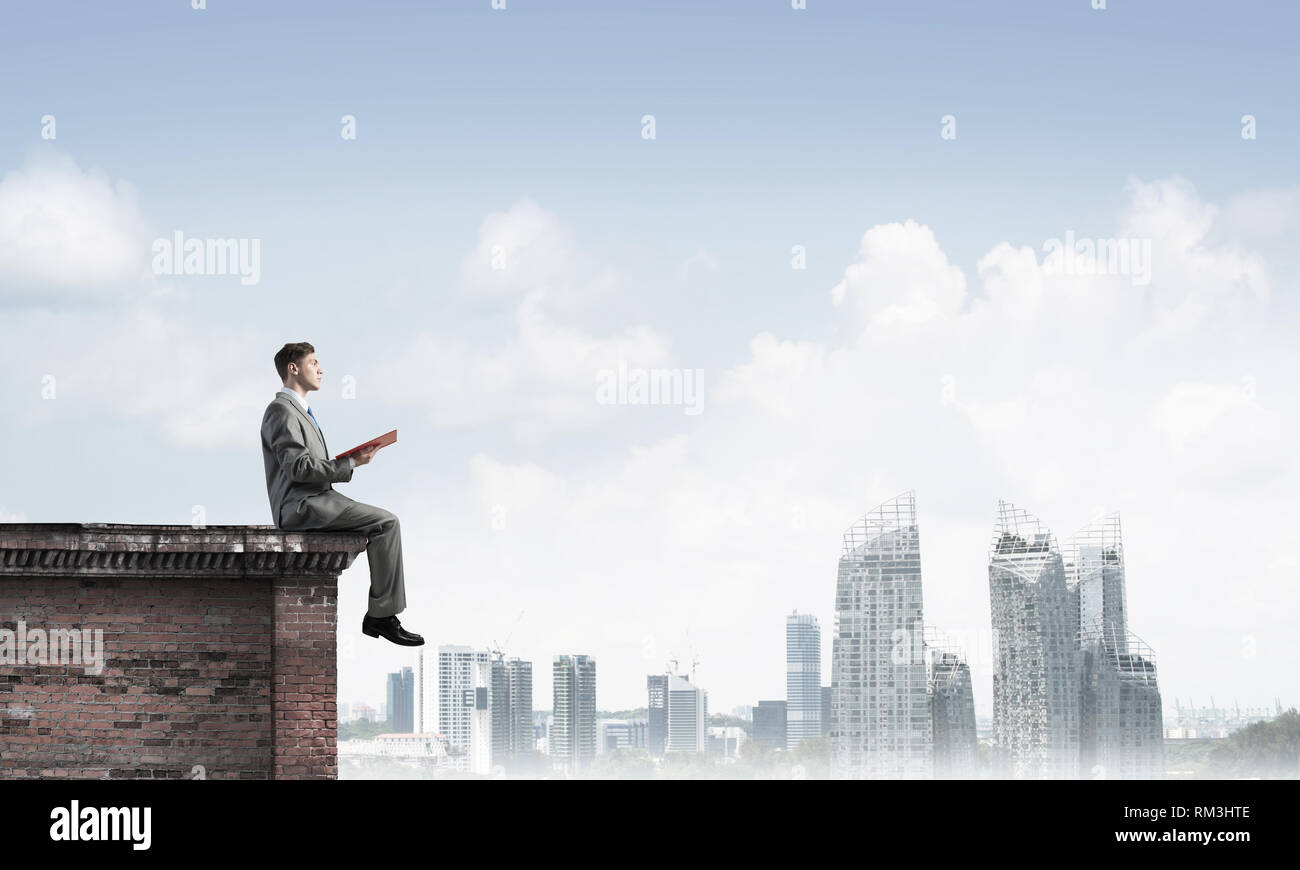 Man on roof edge reading book and cityscape at background Stock Photo ...