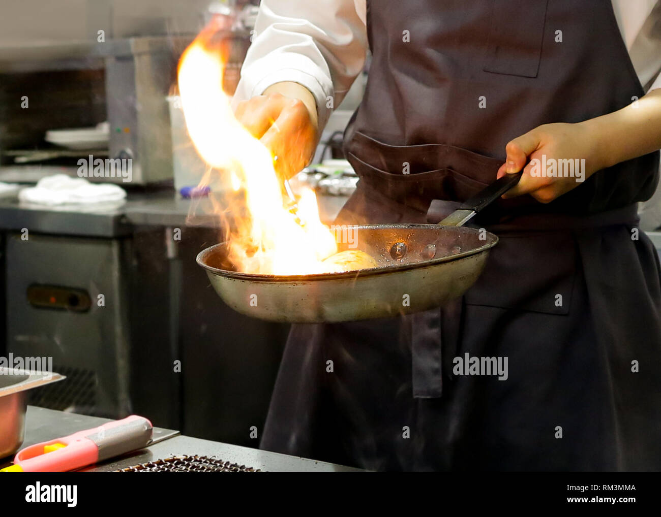 Chef cooking with flame in a frying pan on a kitchen stove, Chef in ...