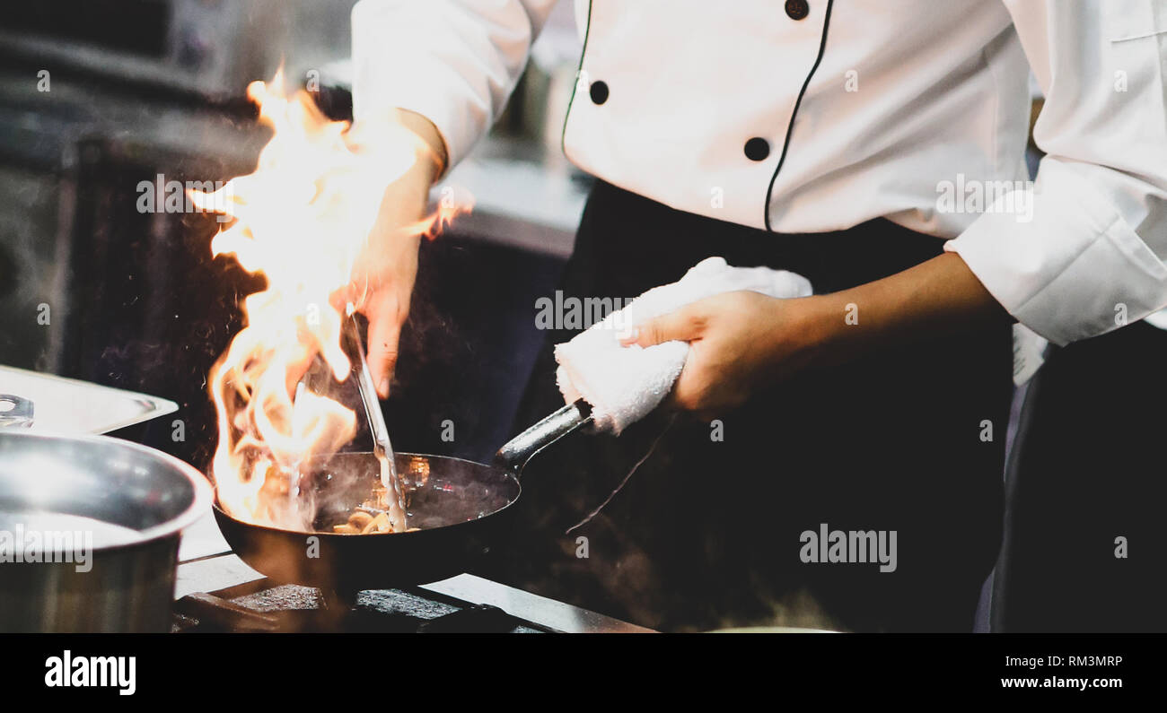 Chef cooking with flame in a frying pan on a kitchen stove, Chef in ...