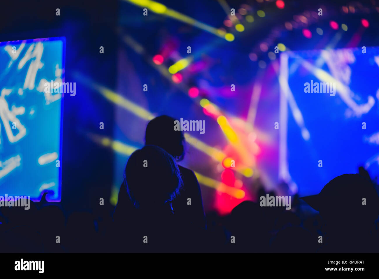 Silhouette of a big crowd at concert against a brightly lit stage ...