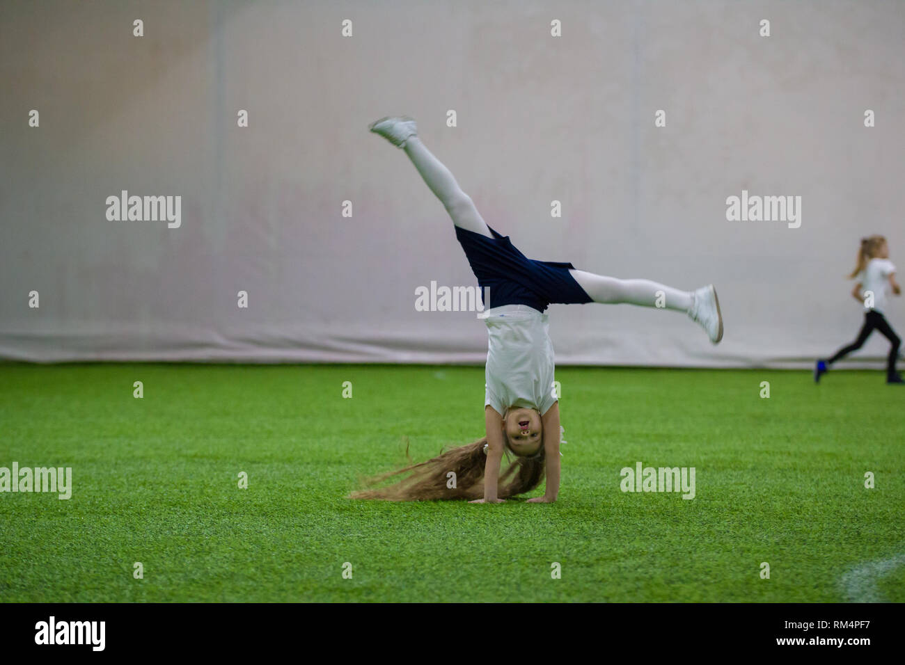A cute little girl with long blonde hair is tumbling on the field Stock ...