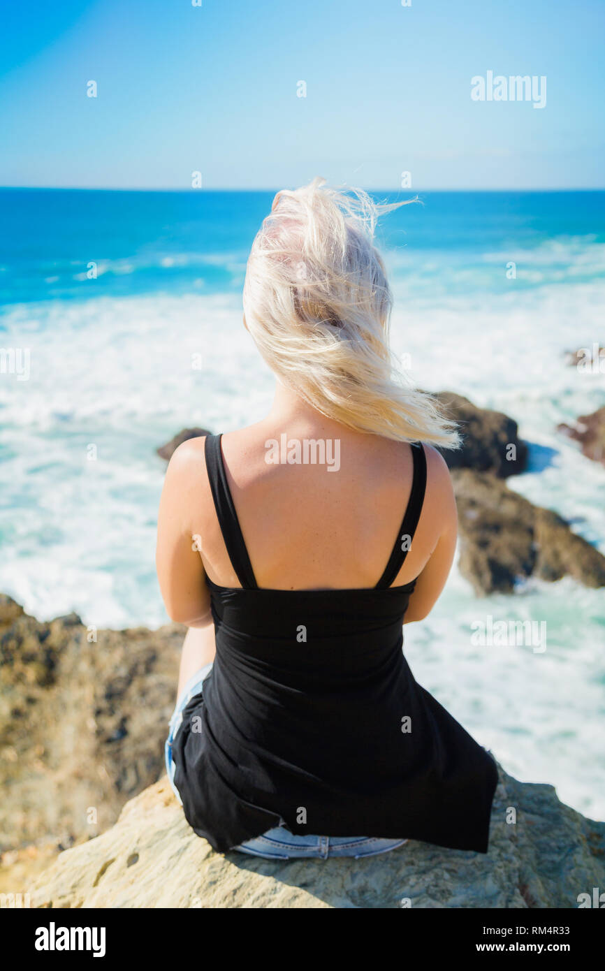 girl sits on a cliff above the ocean back view Stock Photo - Alamy