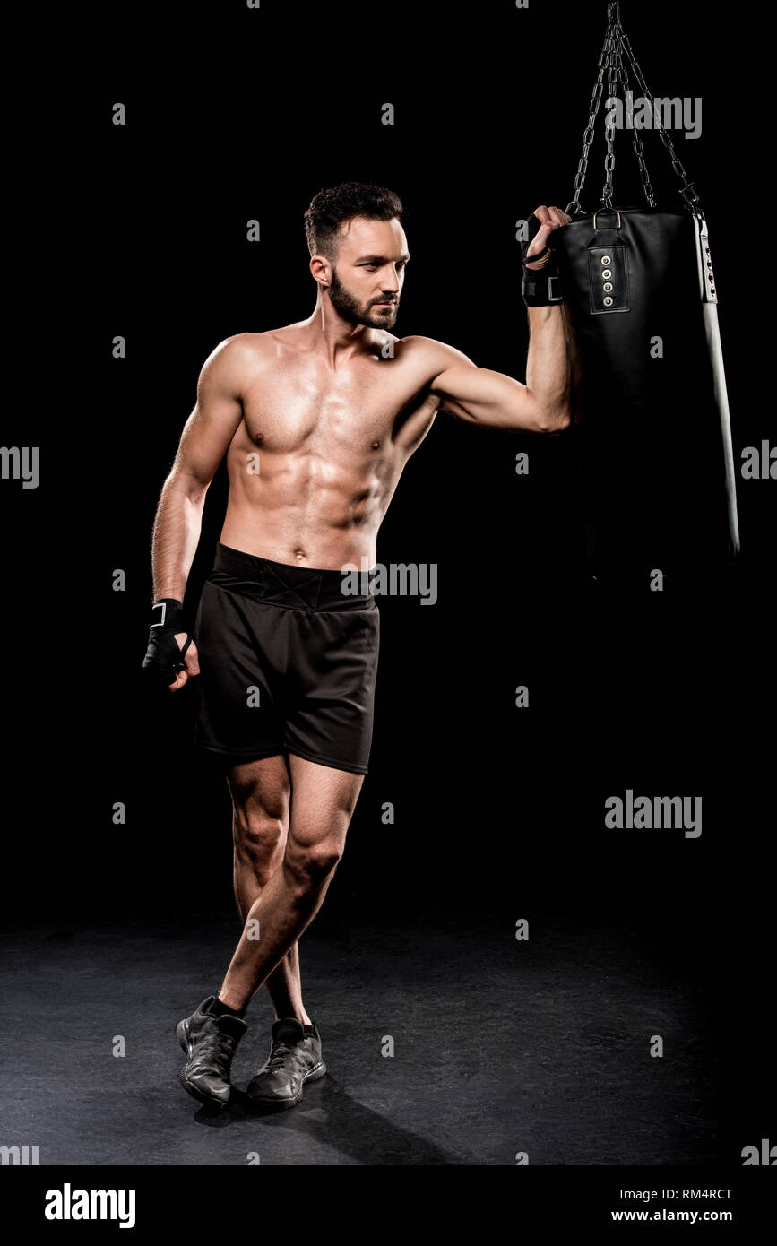 shortless boxer standing with crossed legs near punching bag on black ...