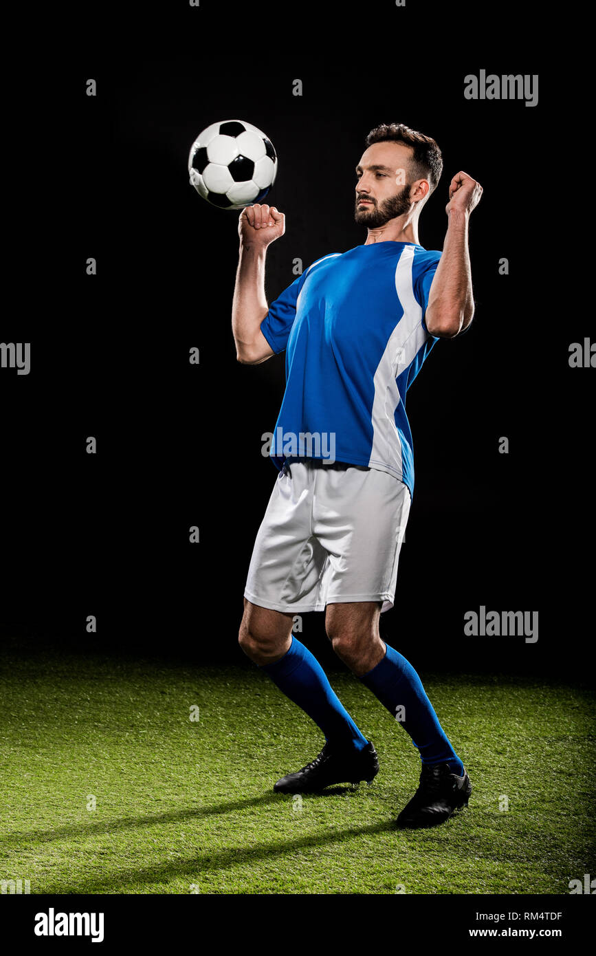 athletic football player in uniform jumping with ball isolated on black ...