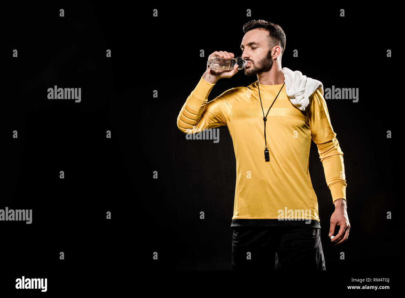 handsome referee drinking water from bottle and standing with towel on ...