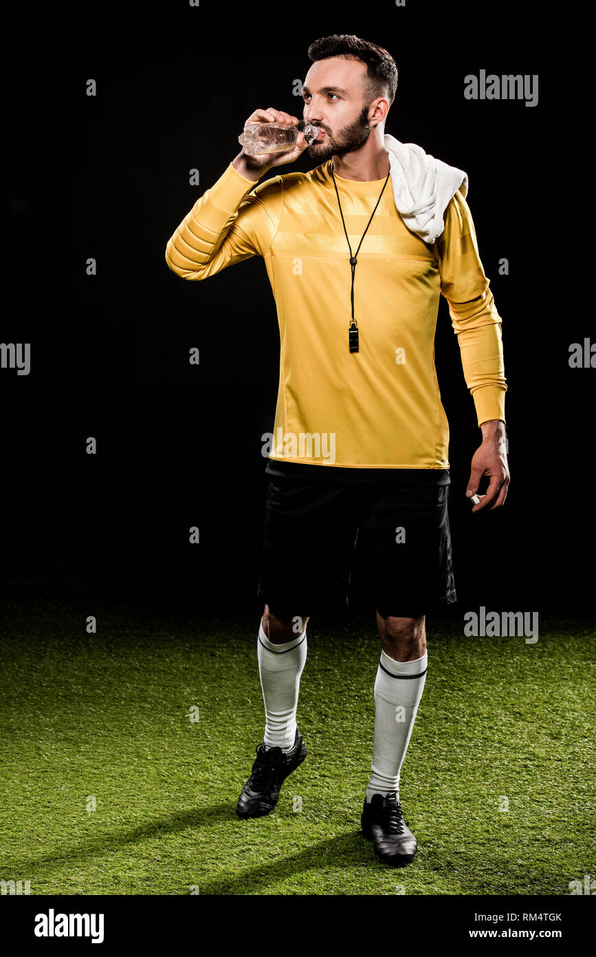 bearded referee drinking water from bottle and standing with towel on ...