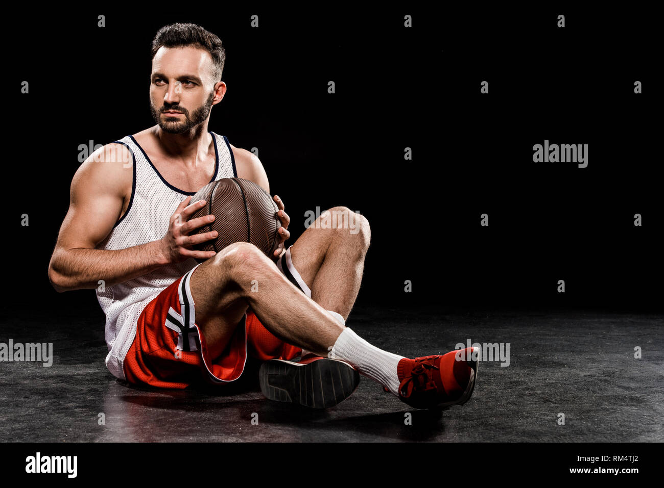muscular basketball player sitting with ball on black background Stock ...