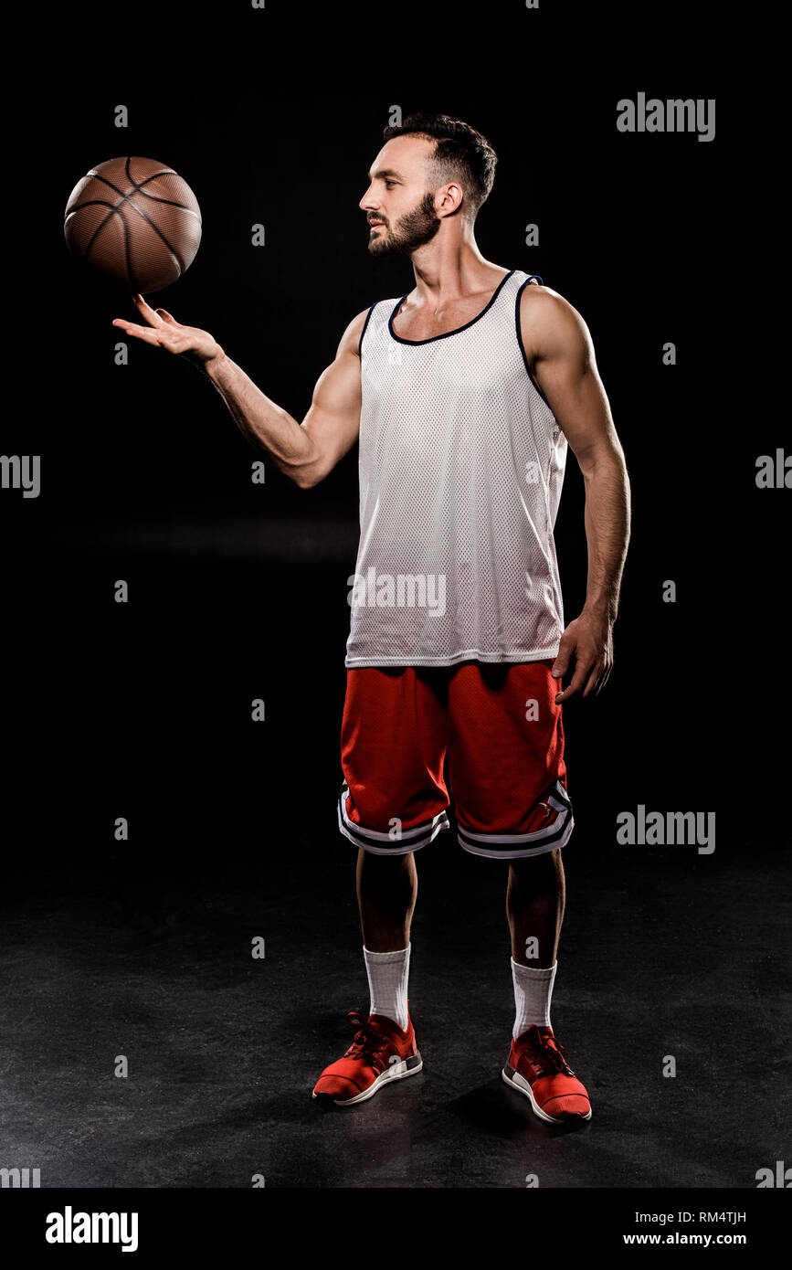 bearded basketball player spinning ball on finger on black background ...