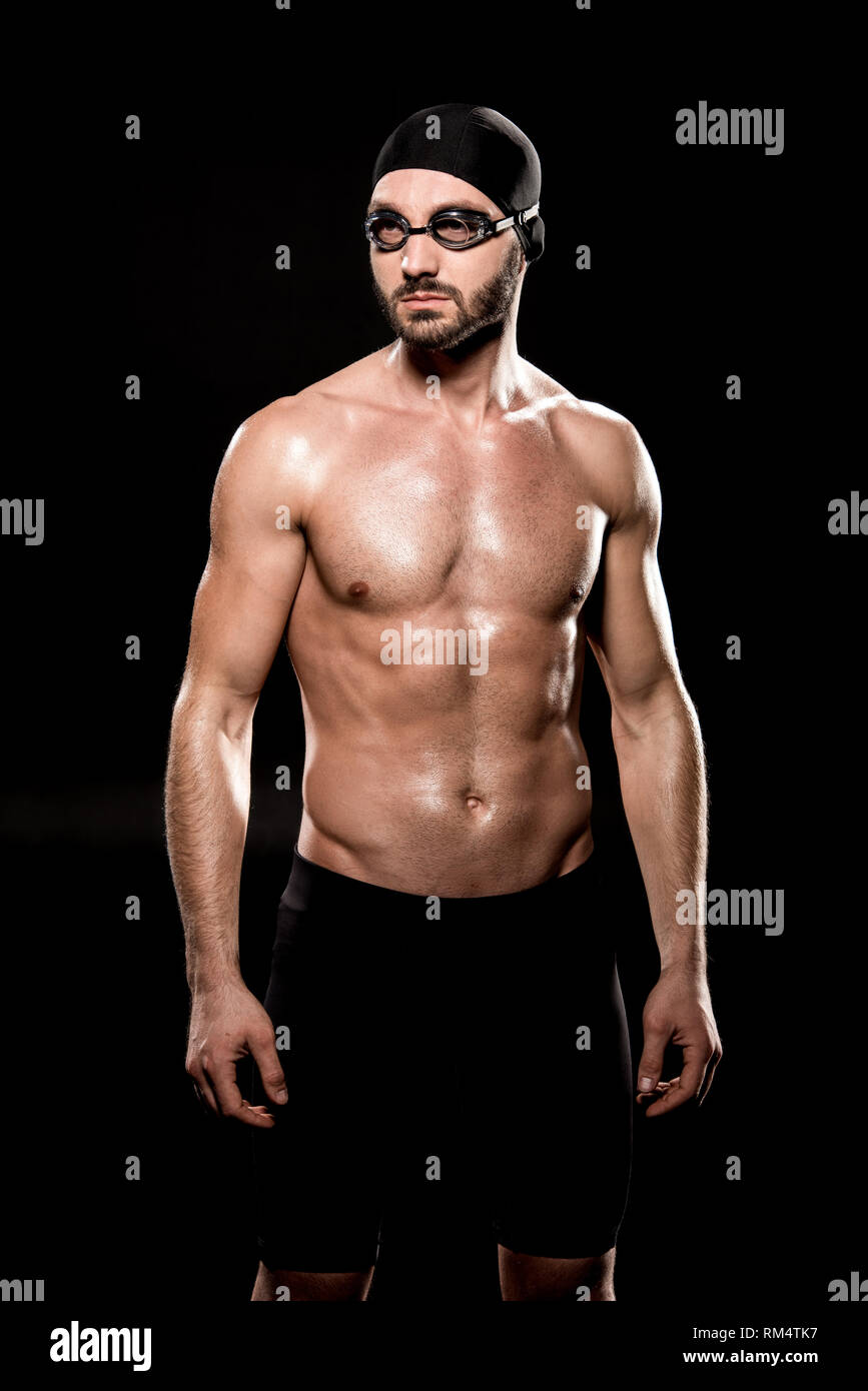 serious swimmer standing in swimming cap and goggles isolated on black ...