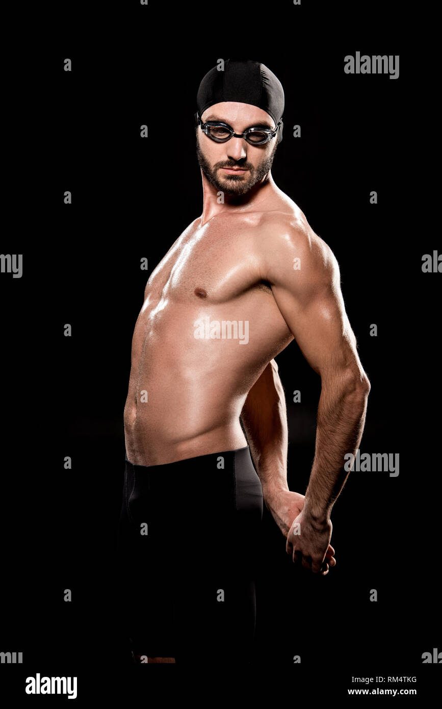 muscular swimmer posing in swimming cap and goggles isolated on black ...