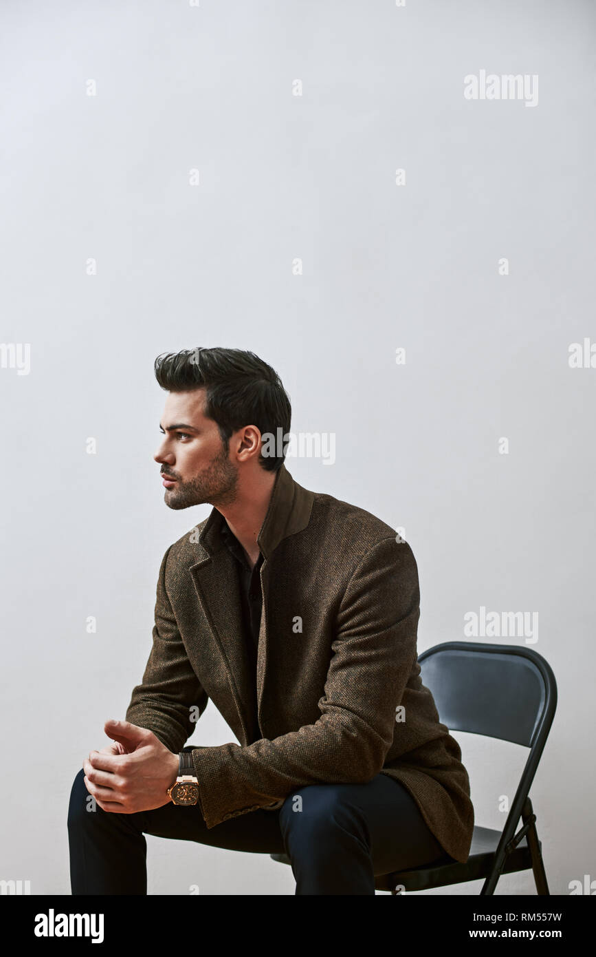 Portrait of a young handsome man wearing brown jacket, sitting on a ...