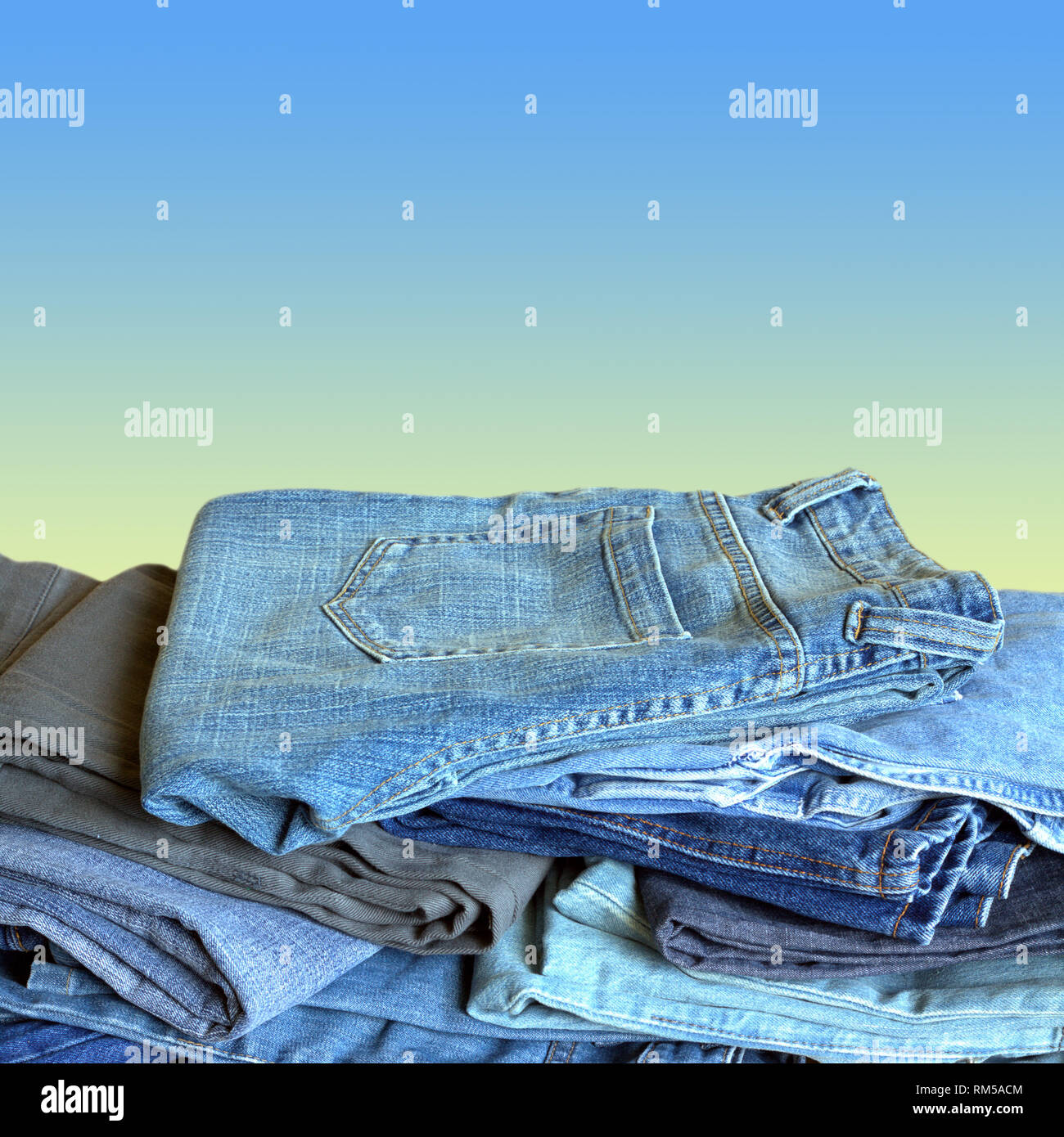 Lot of folded fashion jeans in various colors lie in stacks on gradient ...