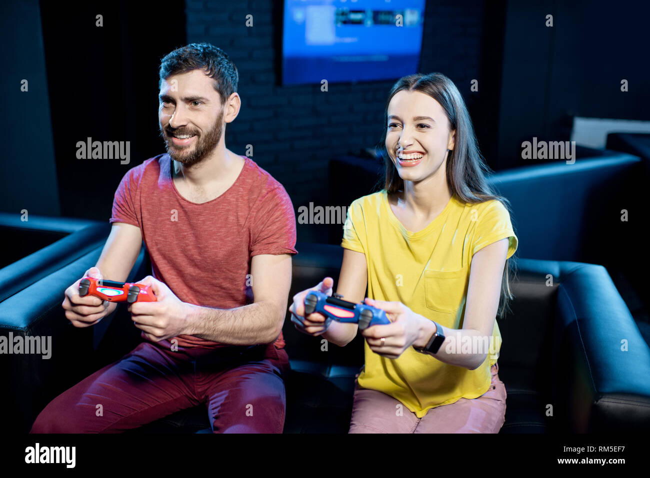 Young couple playing video games with gaming console sitting together ...