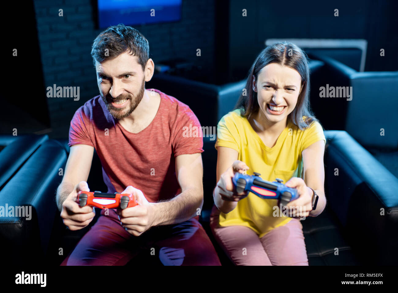 Young couple playing video games with gaming console sitting together ...