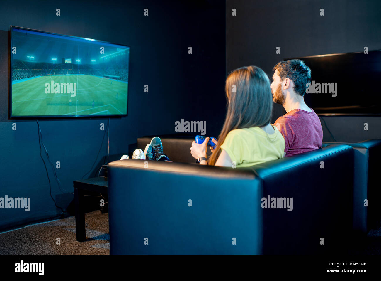 Young couple playing football game with gaming console sitting on the ...