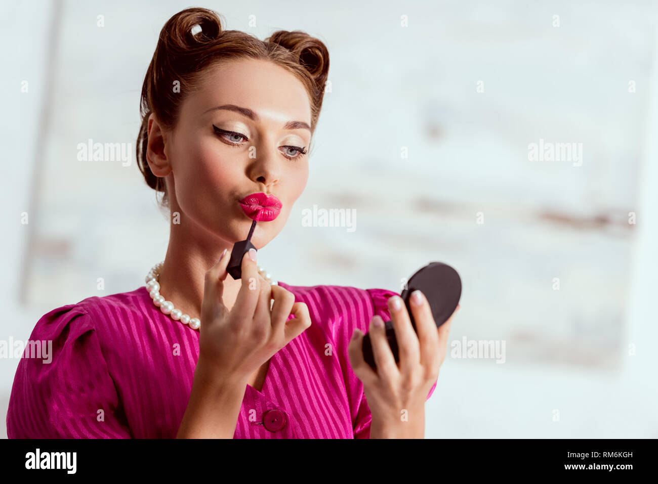 Beautiful pin up girl looking at face powder mirror and using lip balm ...