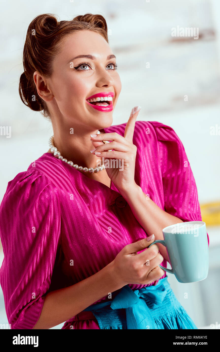 Stylish pin up girl in crimson dress and blue apron holding coffee cup ...