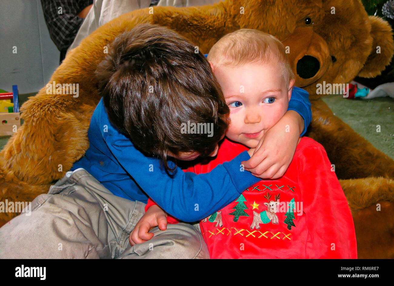 young boy hugs toddler boy; large stuffed bear; love; affection ...