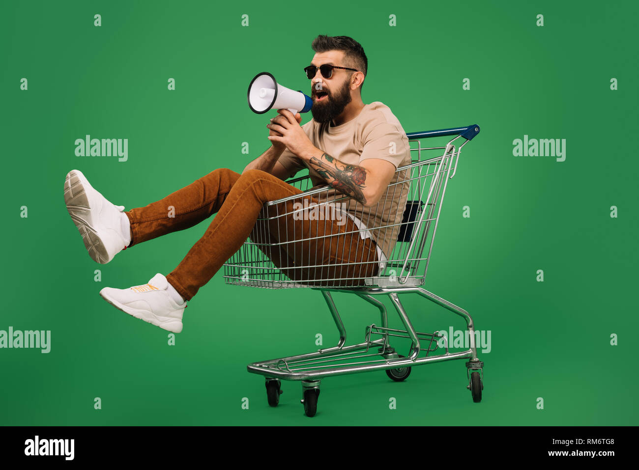 bearded man with megaphone sitting in shopping cart isolated on green ...