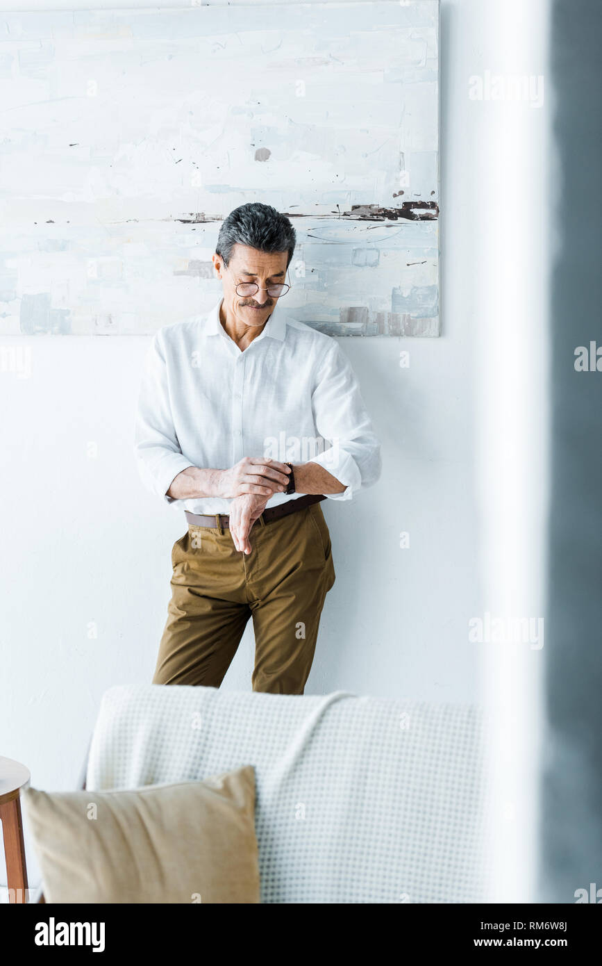 senior man in glasses looking at watch in living room Stock Photo - Alamy