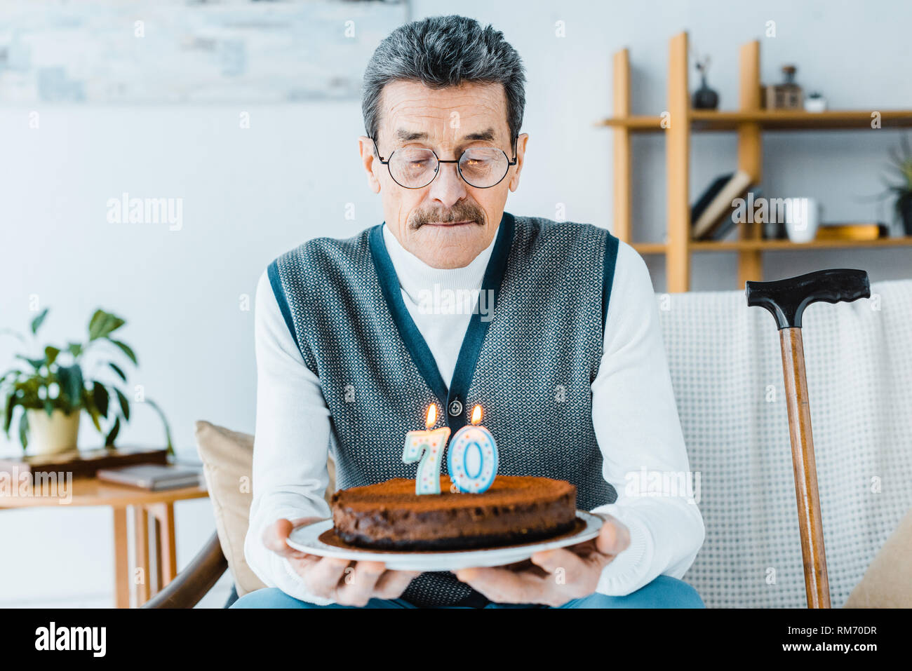 sad senior man holding birthday cake while sitting on sofa a in living ...