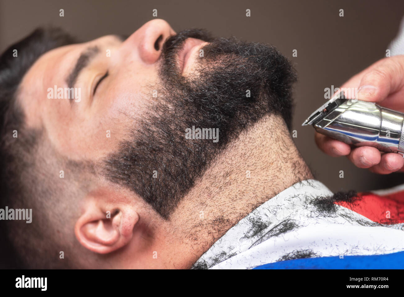 Barber shaving the beard of a handsome bearded man with an electric ...