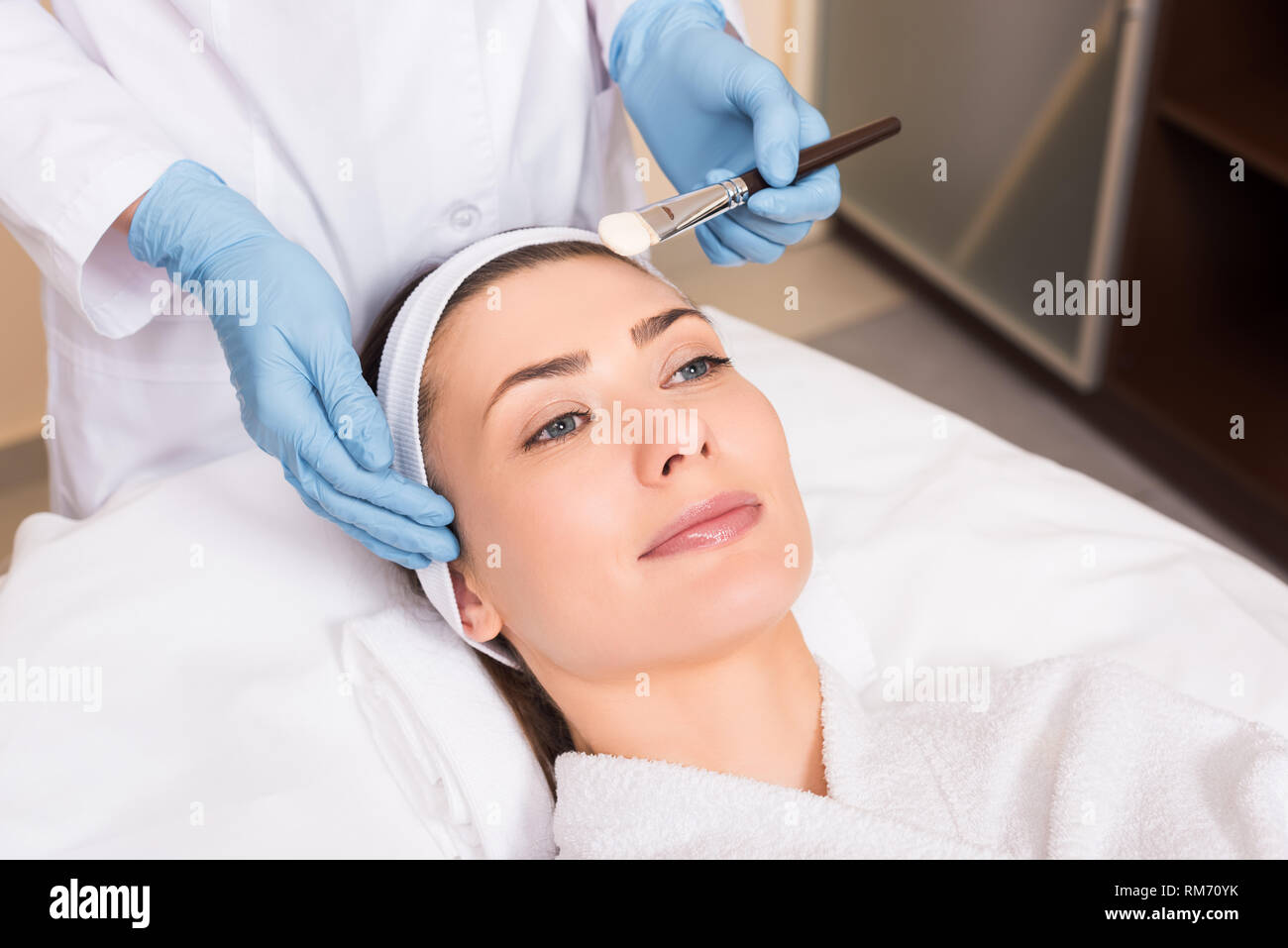 beautician applying cosmetic mask on woman forehead at beauty salon ...