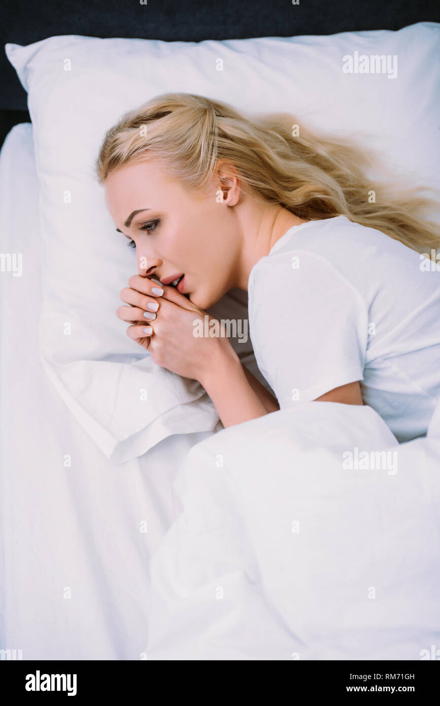 selective focus of scared woman with folded hands lying in bed at home ...