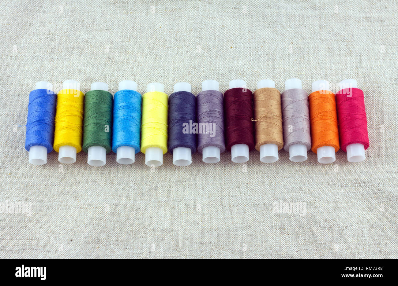 Long horizontal row of lot color thread spools on beige fabric ...